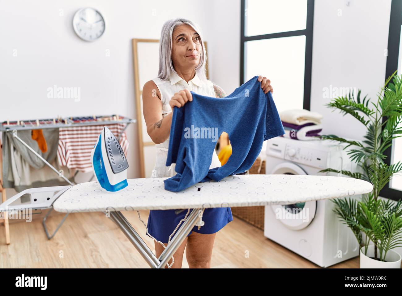Middle age grey-haired woman ironing holding burned iron shirt at ...