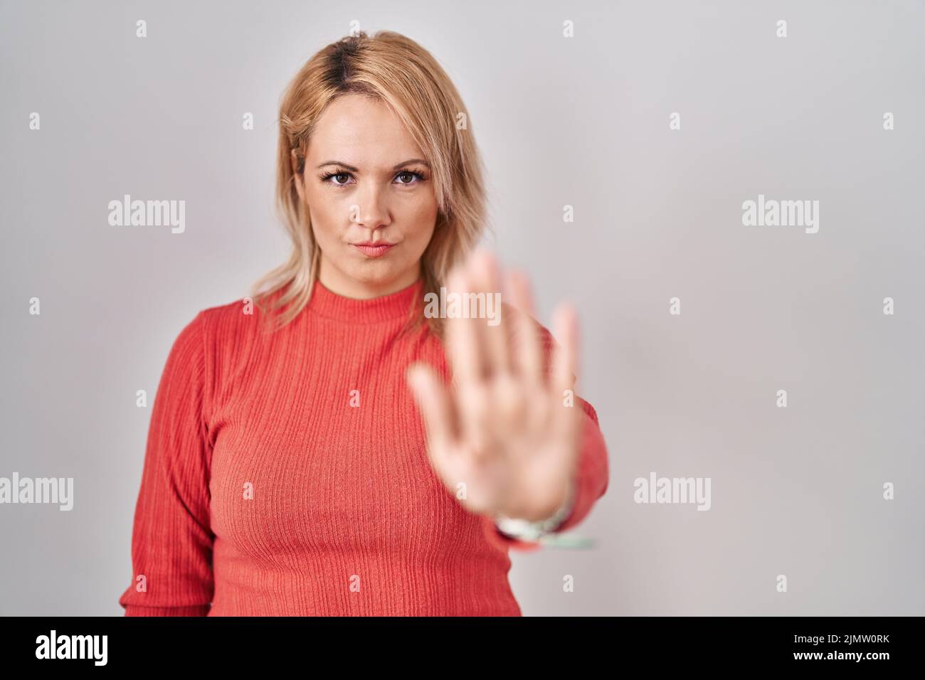 Blonde woman standing over isolated background doing stop sing with ...
