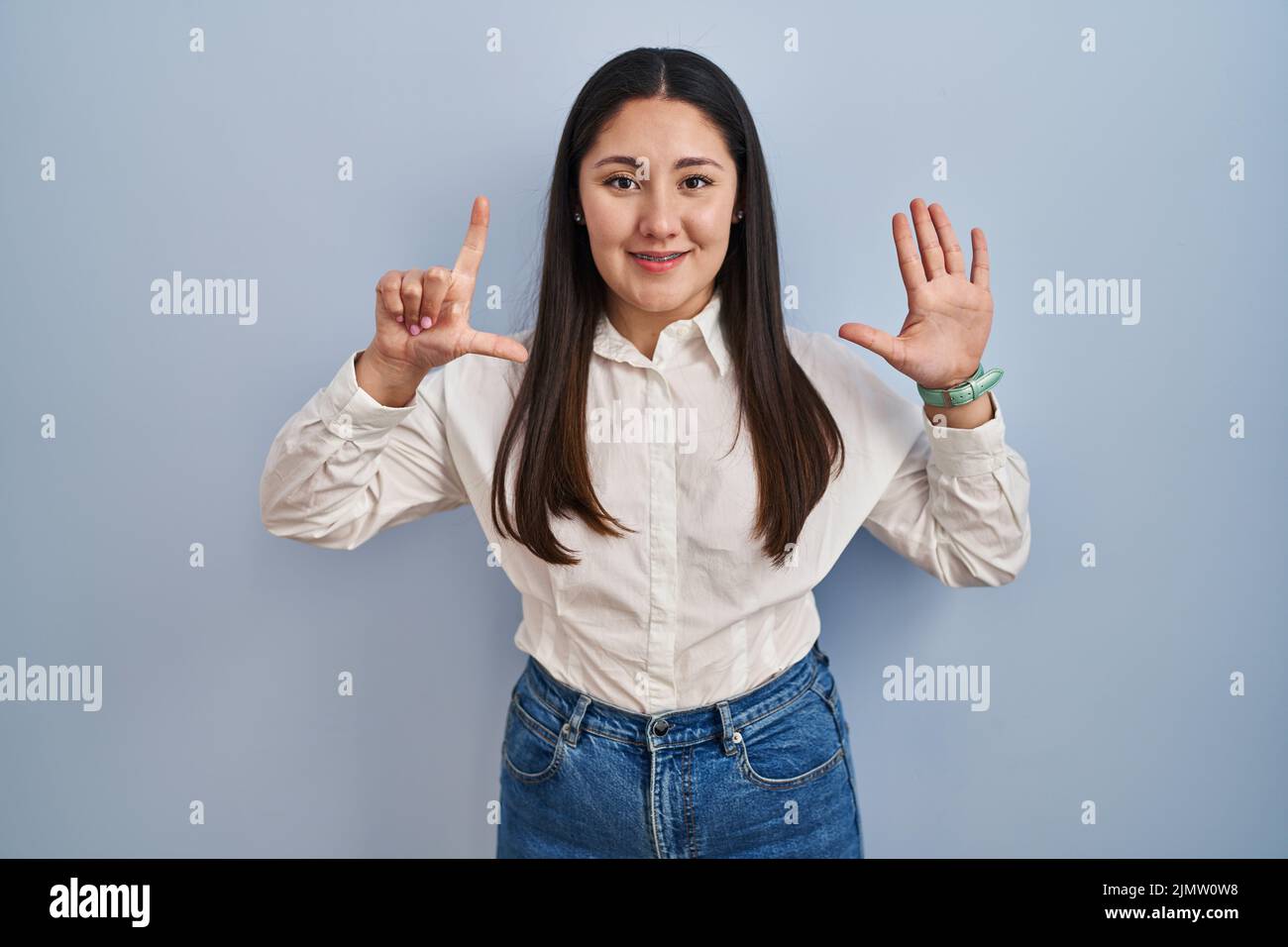 Young latin woman standing over blue background showing and pointing up ...
