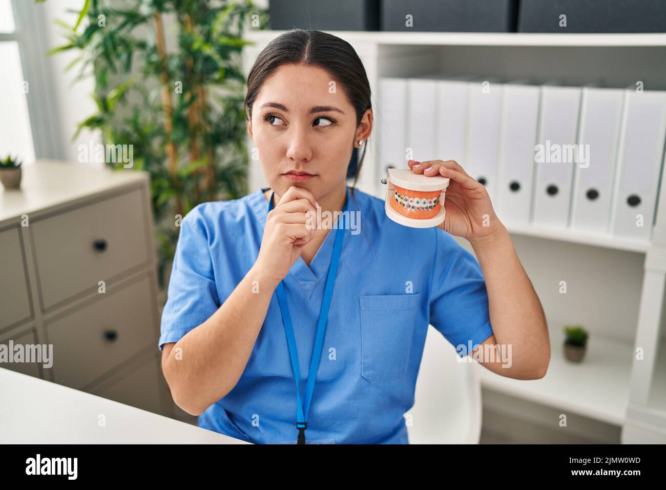 Young latin dentist woman holding denture with braces serious face ...