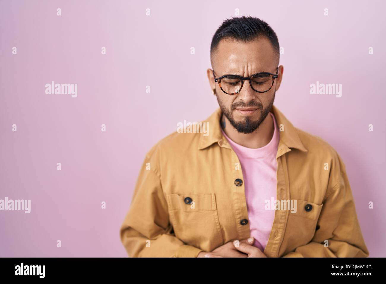 Young hispanic man standing over pink background with hand on stomach ...