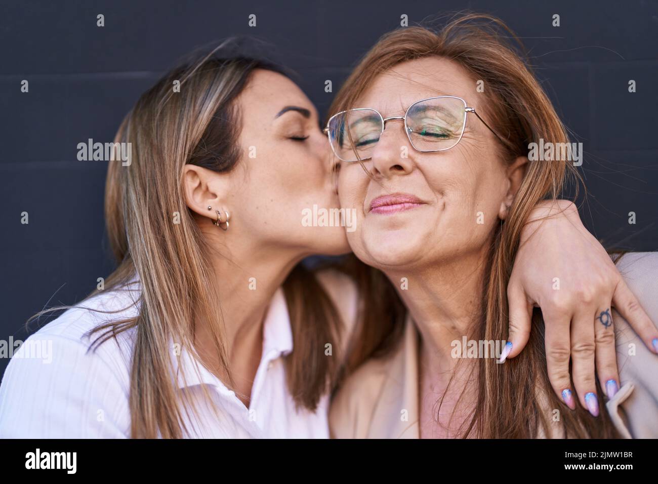 Mother and daughter smiling confident hugging each other and kissing over black background Stock ...
