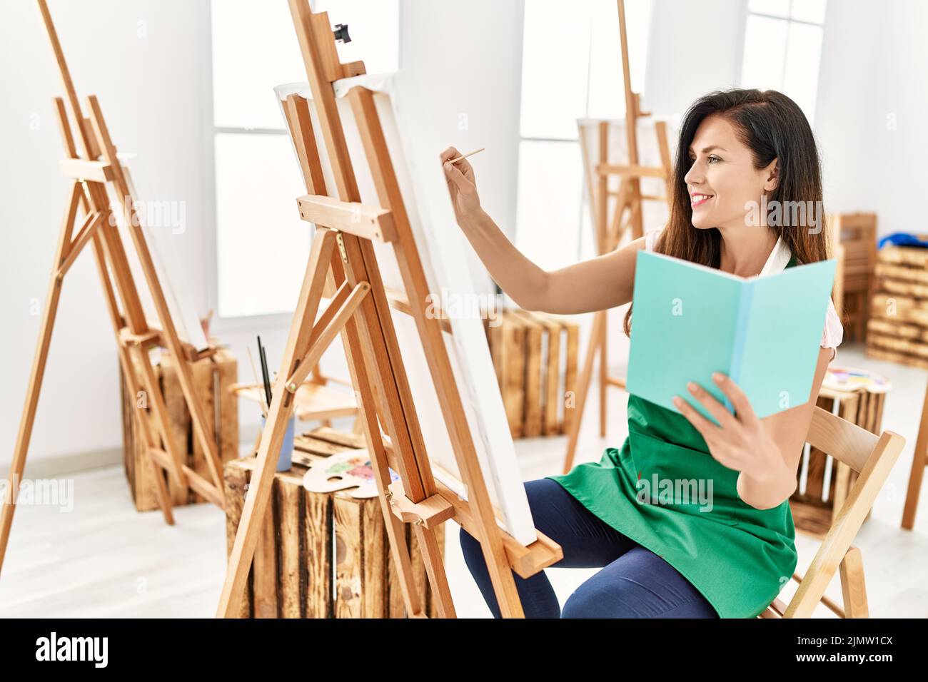 Middle age hispanic woman looking book drawing at art studio Stock ...