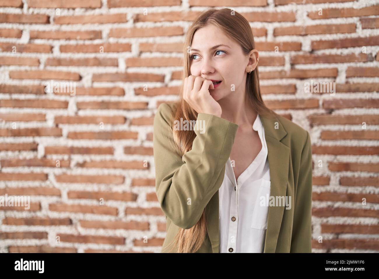Young caucasian woman standing over bricks wall background looking ...