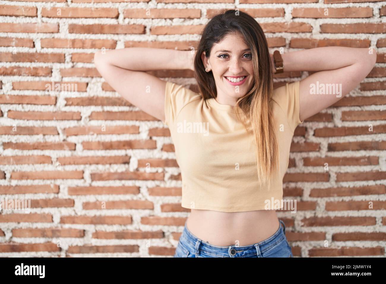 Young brunette woman standing over bricks wall relaxing and stretching ...
