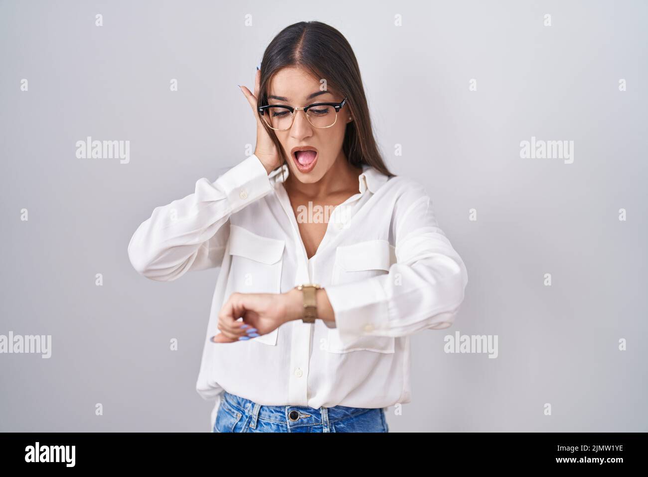 Young brunette woman wearing glasses looking at the watch time worried ...
