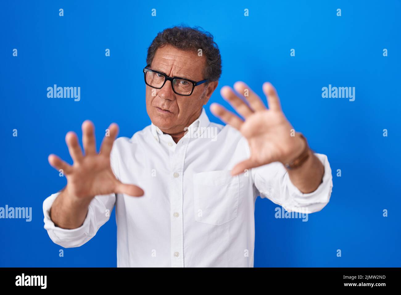 Middle age hispanic man standing over blue background afraid and ...