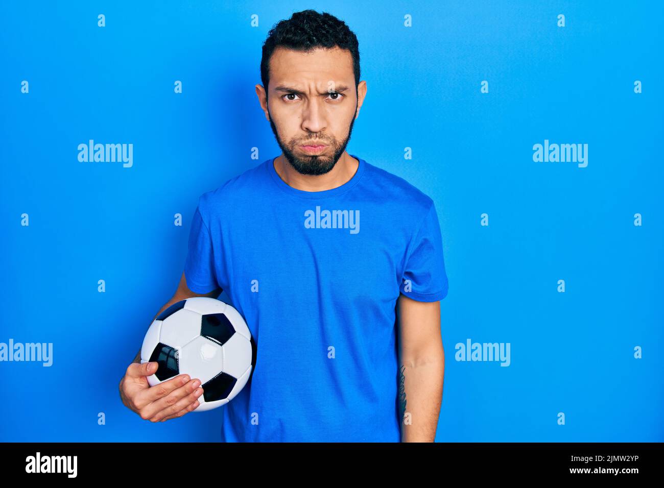 Hispanic man with beard holding soccer ball puffing cheeks with funny ...