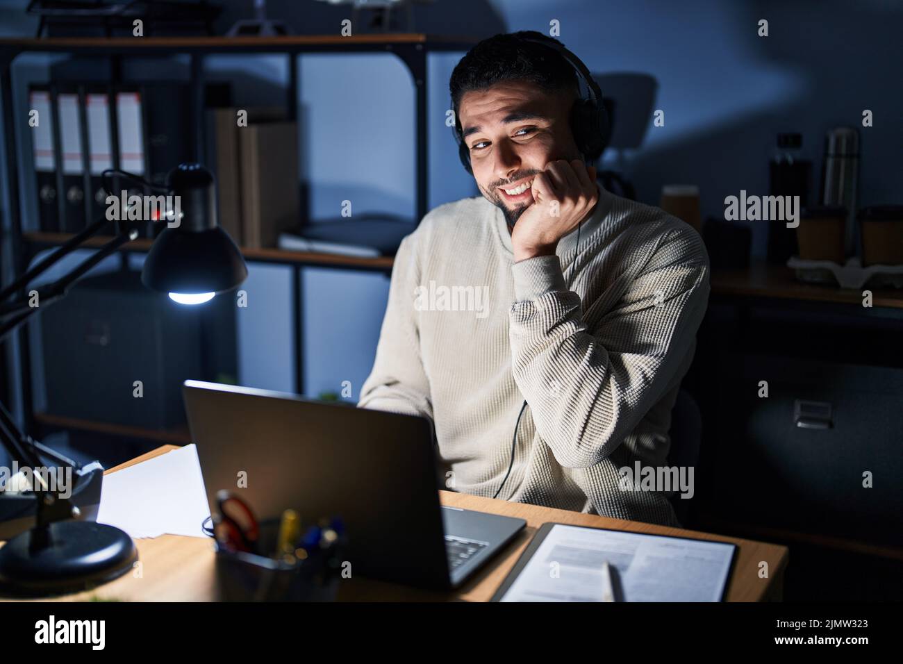 Young handsome man working using computer laptop at night looking ...