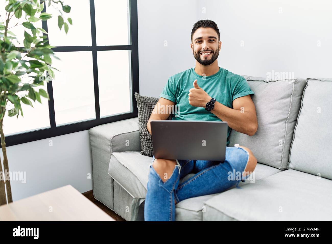 Young handsome man with beard using computer laptop sitting on the sofa ...