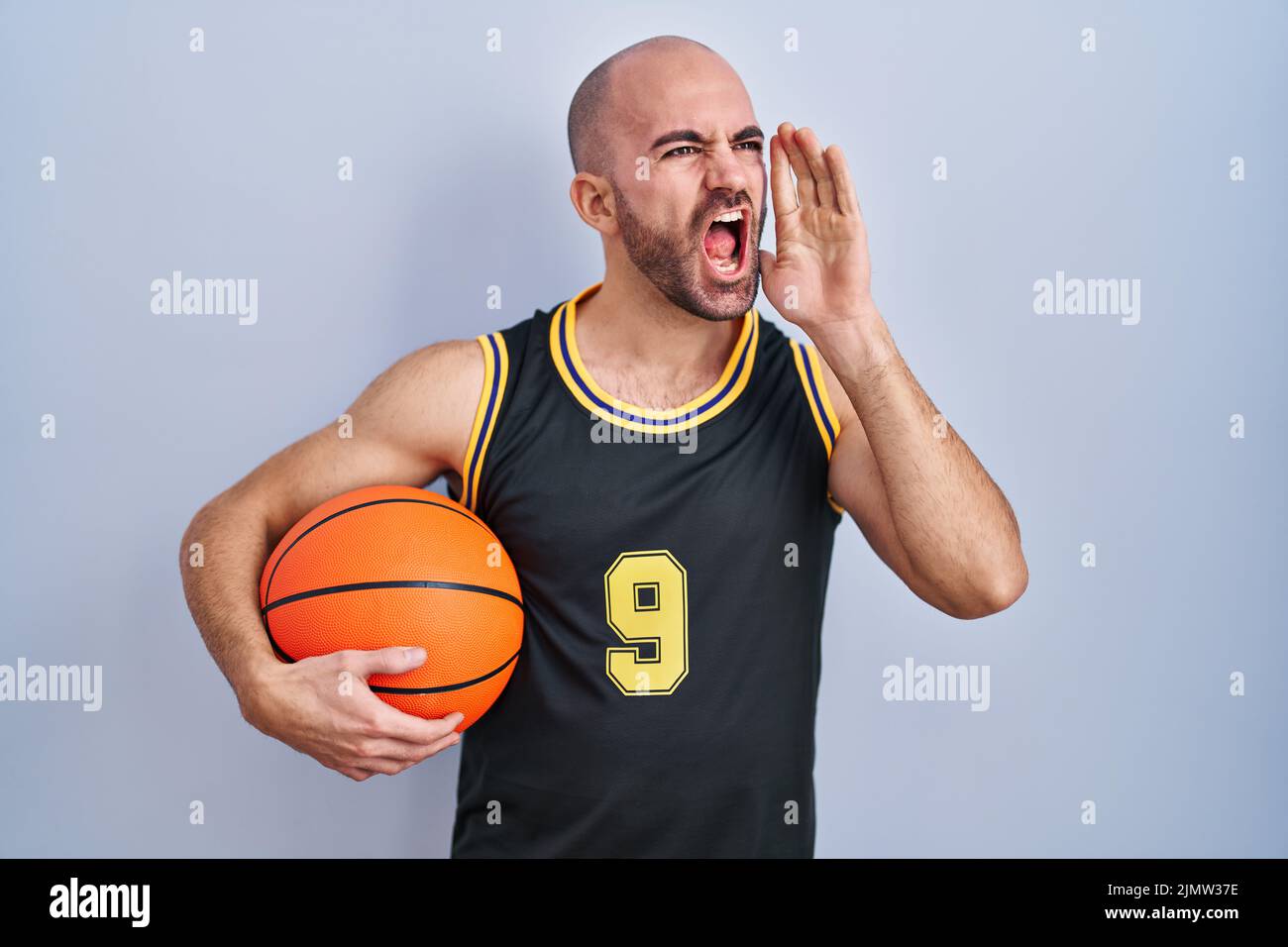 Young bald man with beard wearing basketball uniform holding ball ...