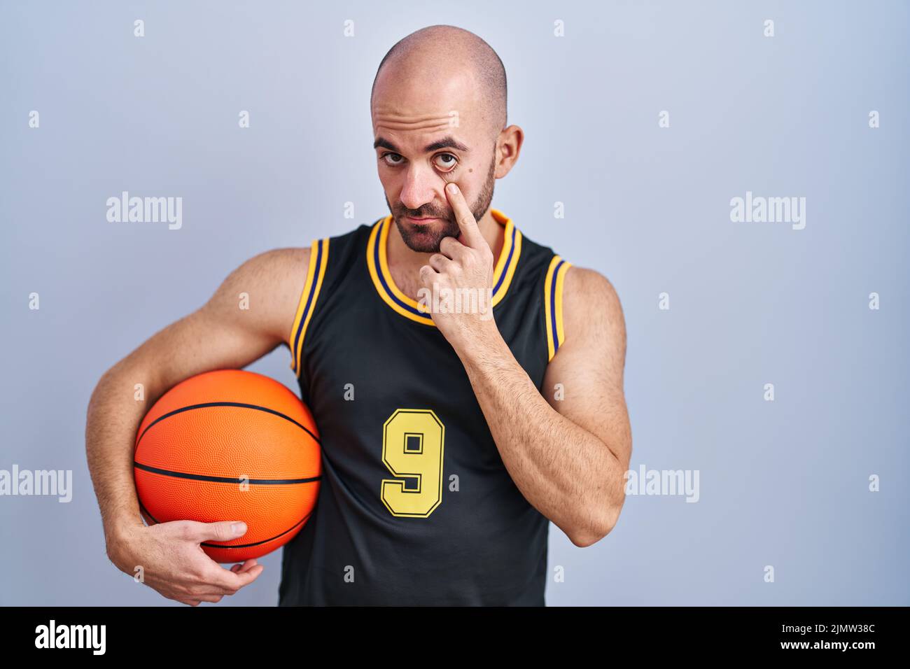 Young bald man with beard wearing basketball uniform holding ball ...