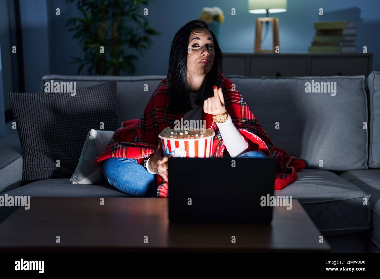Hispanic woman eating popcorn watching a movie on the sofa doing money ...