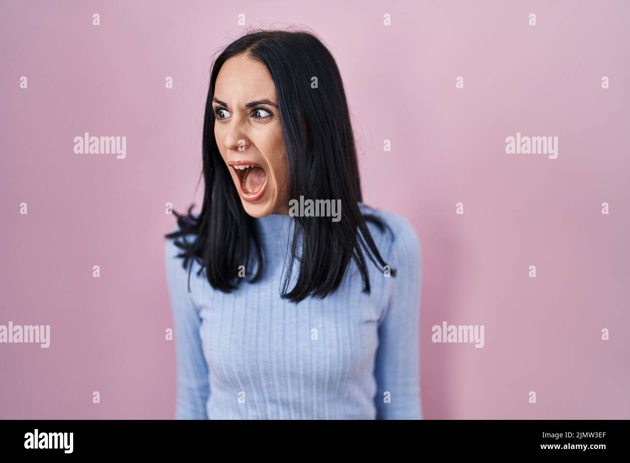 Hispanic woman standing over pink background angry and mad screaming ...
