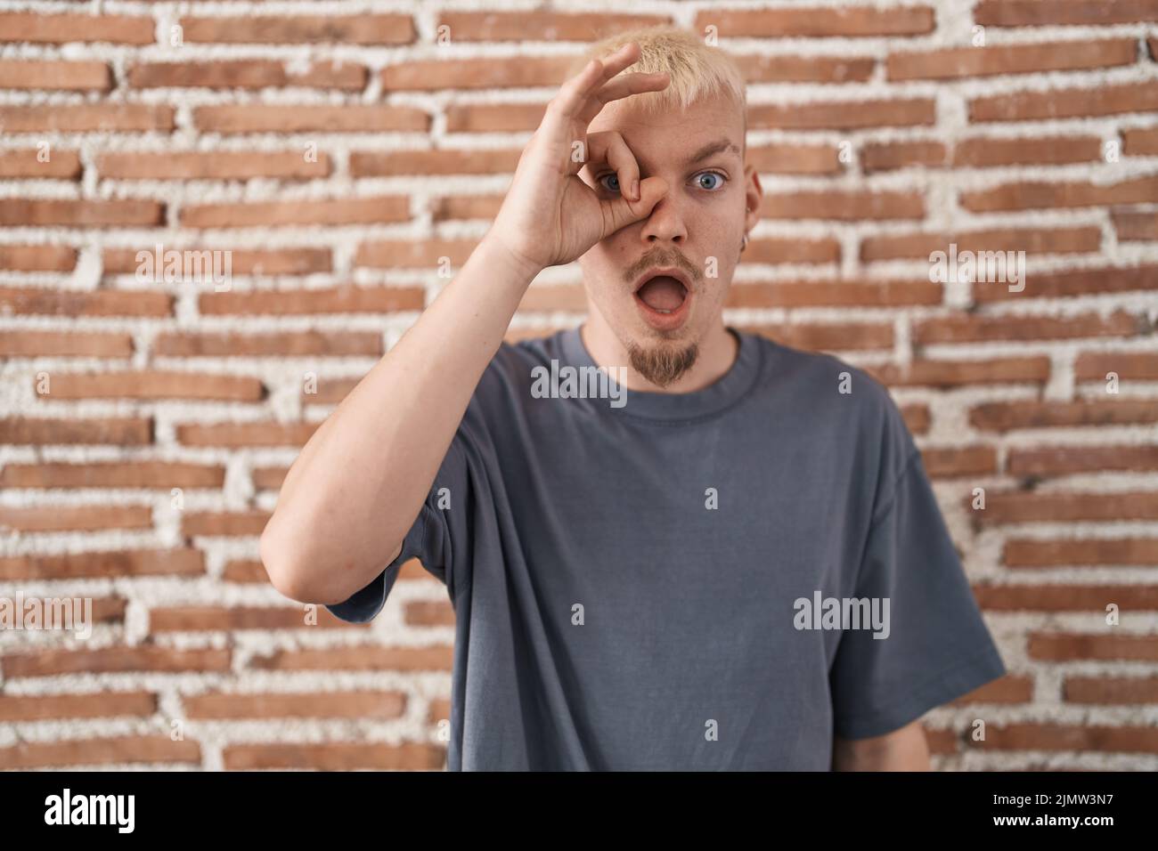 Young caucasian man standing over bricks wall doing ok gesture shocked ...