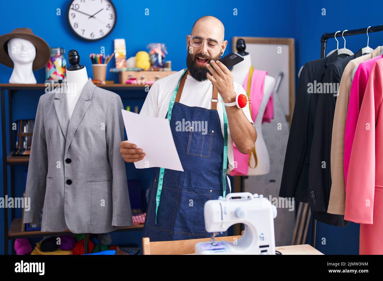 Young bald man tailor talking on smartphone looking clothing design at ...