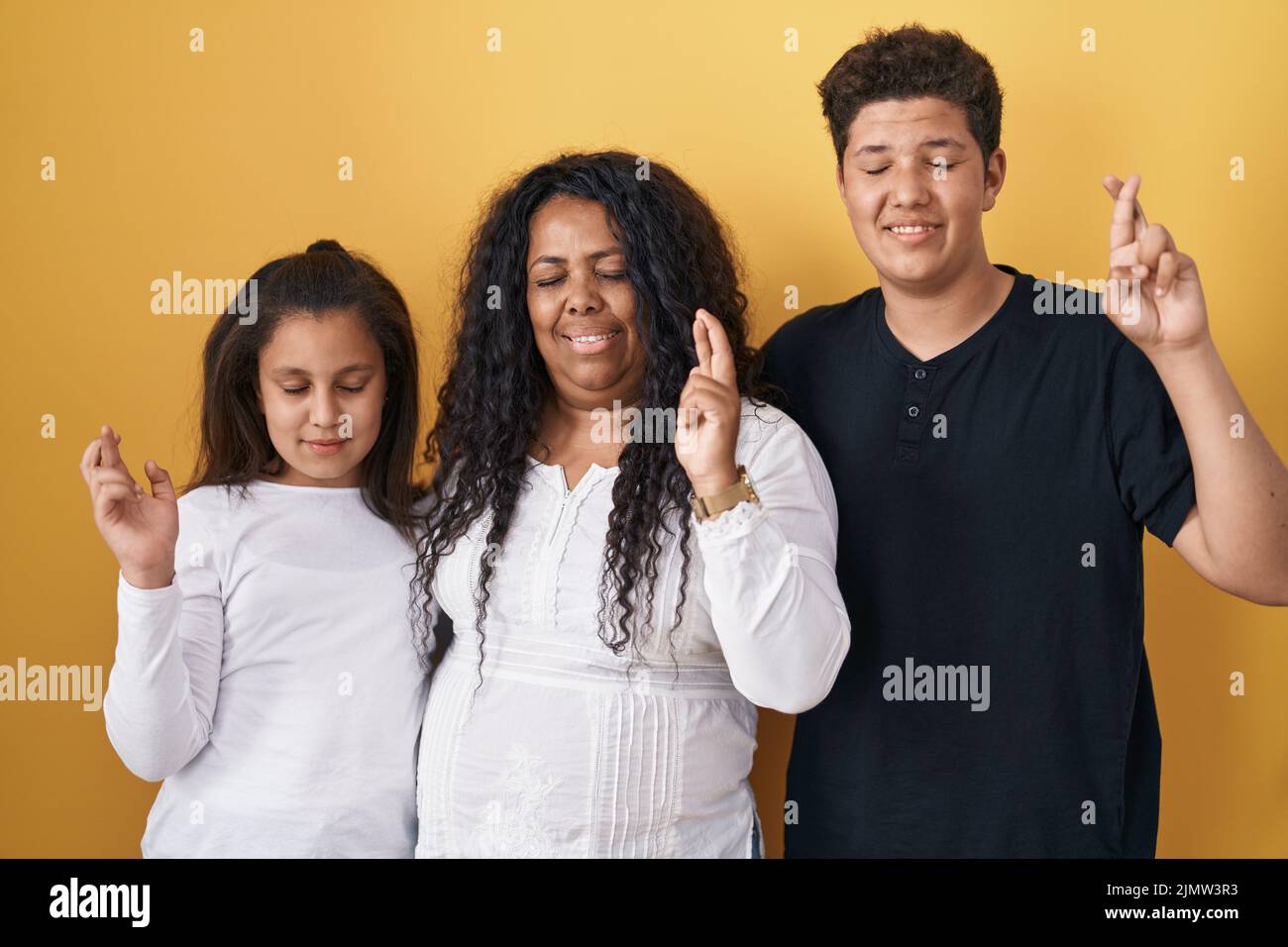 Family of mother, daughter and son standing over yellow background ...