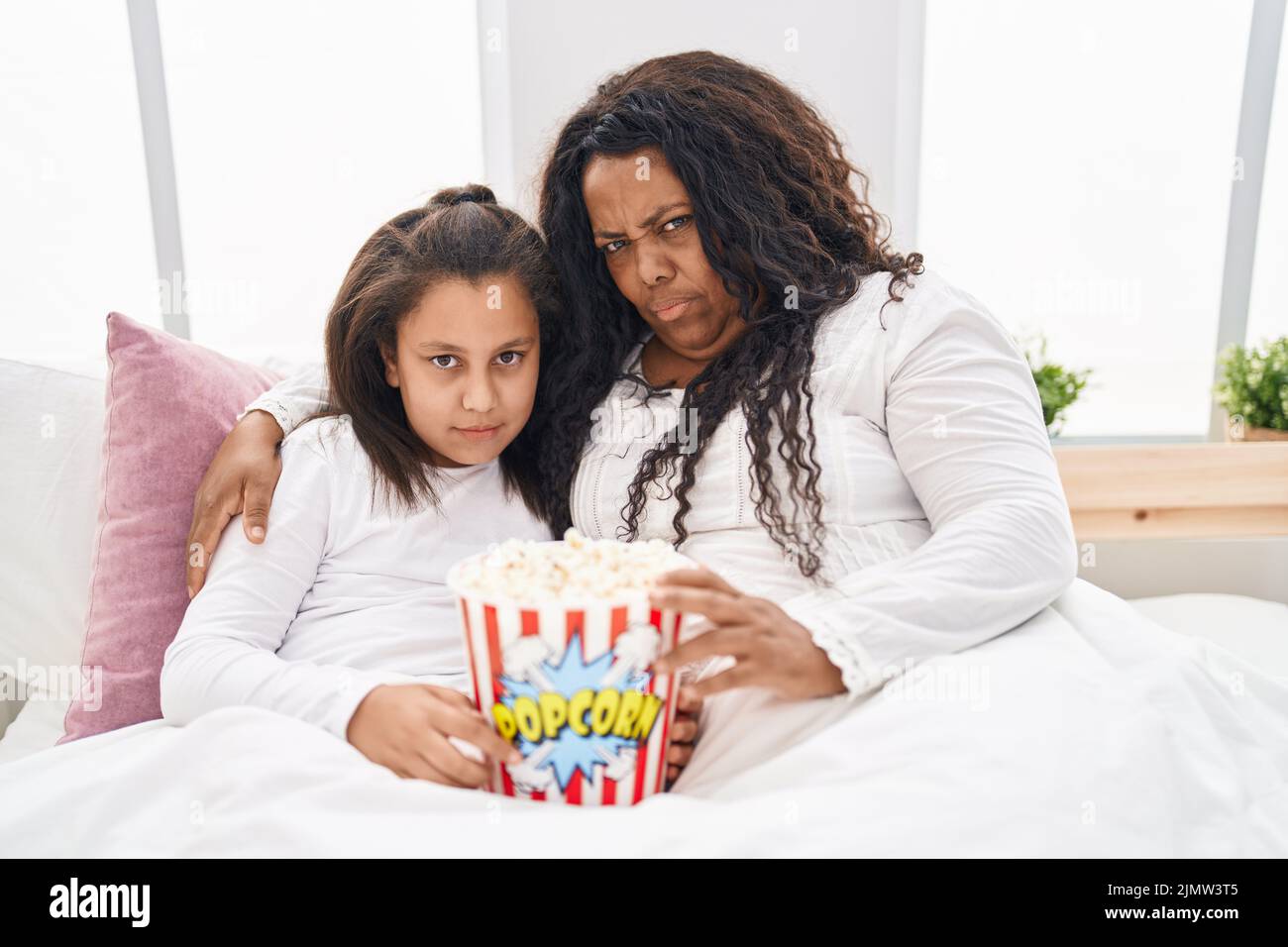 Mother and young daughter eating popcorn in the bed skeptic and nervous ...