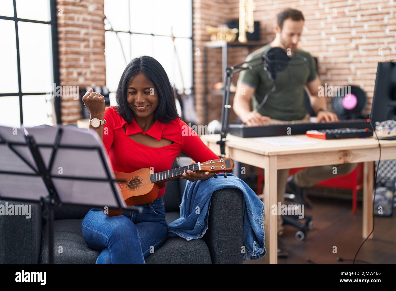 Young indian woman playing ukulele at music studio screaming proud ...