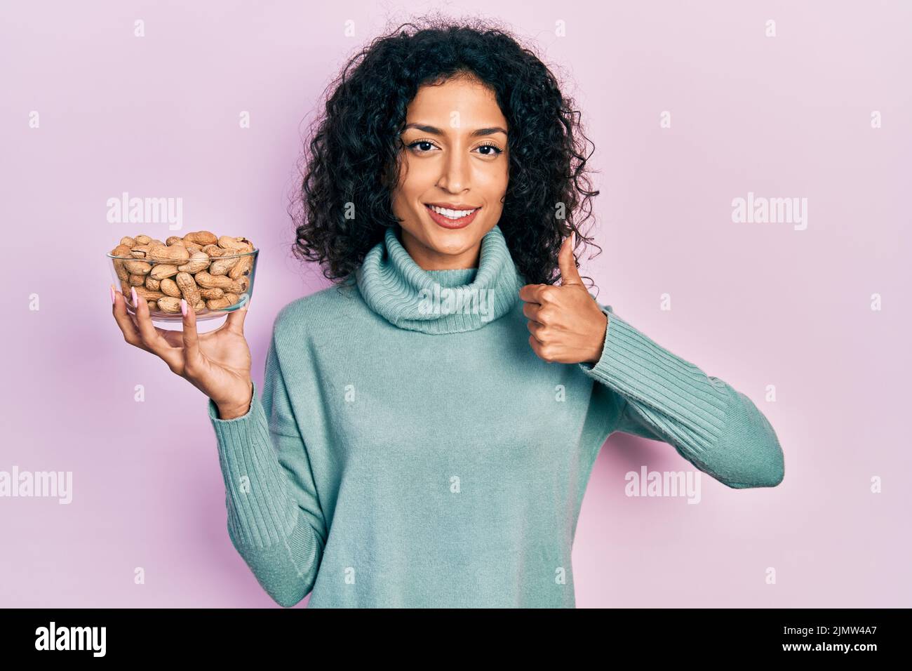 Young latin girl holding peanuts smiling happy and positive, thumb up ...