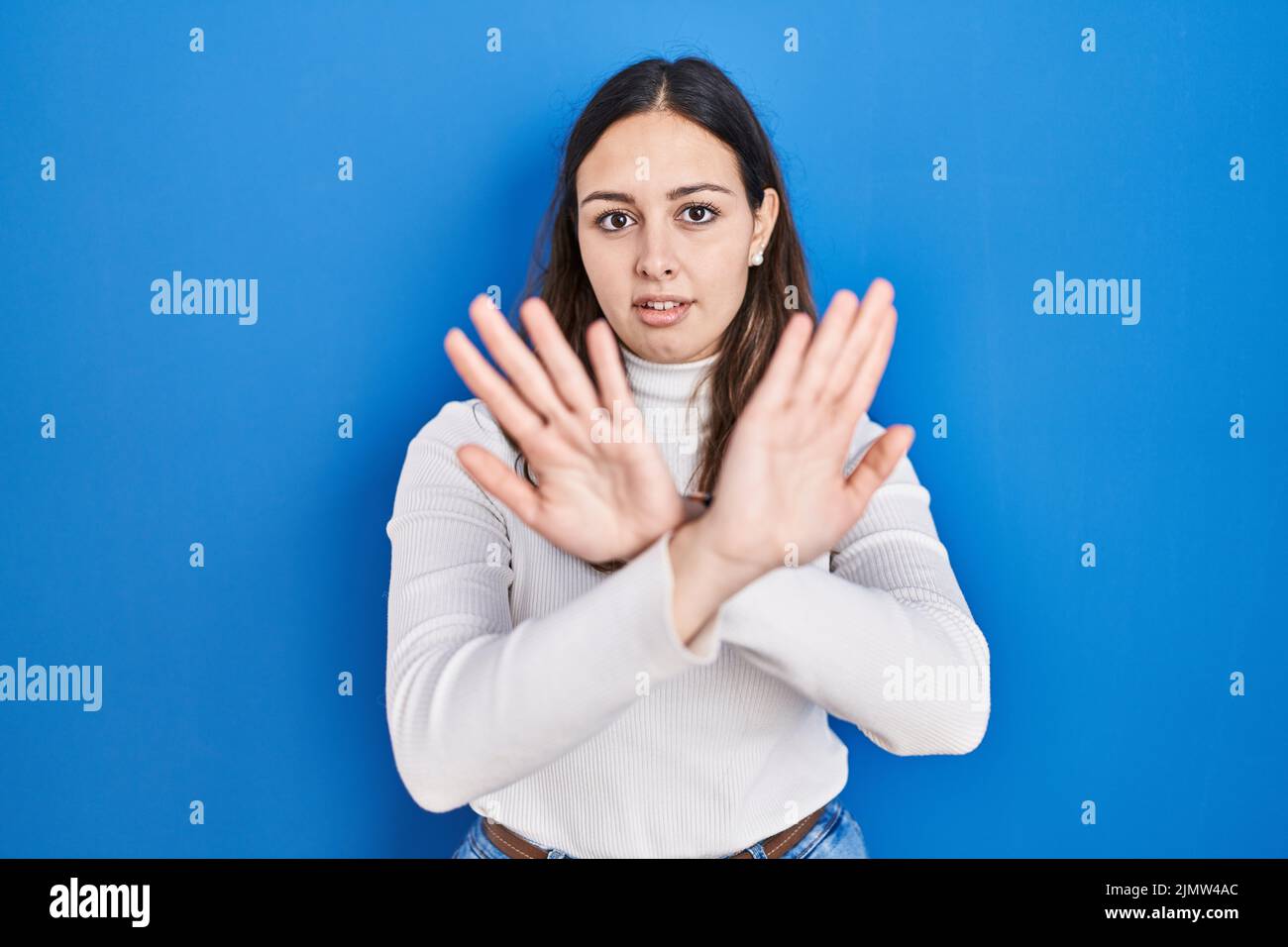 Young hispanic woman standing over blue background rejection expression ...