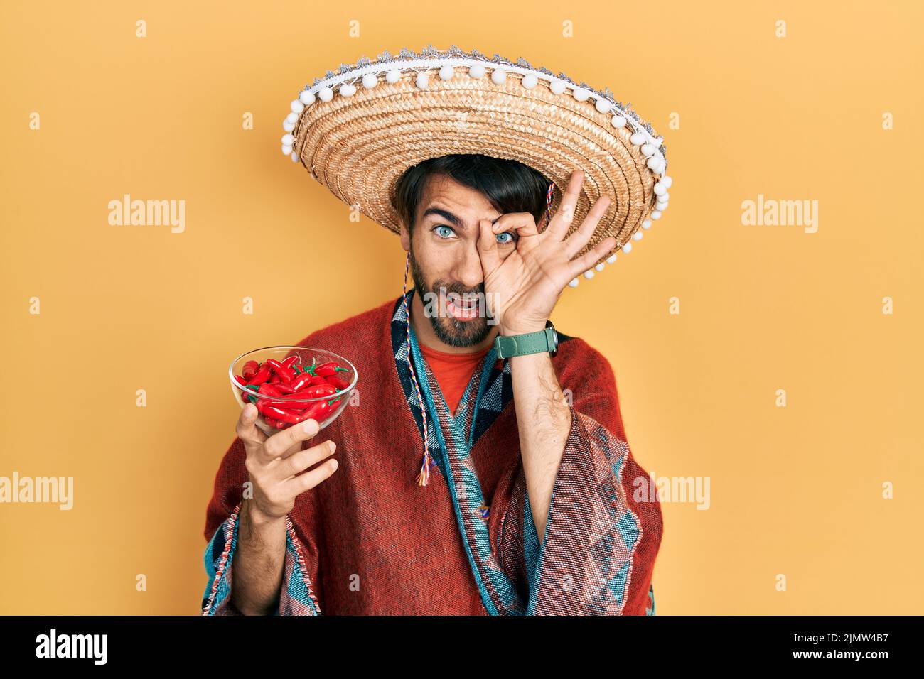 Young hispanic man wearing mexican hat holding chili smiling happy ...