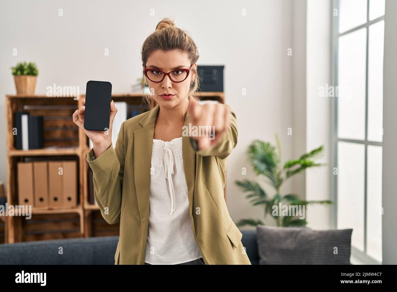 Young woman working at consultation office holding smartphone pointing ...