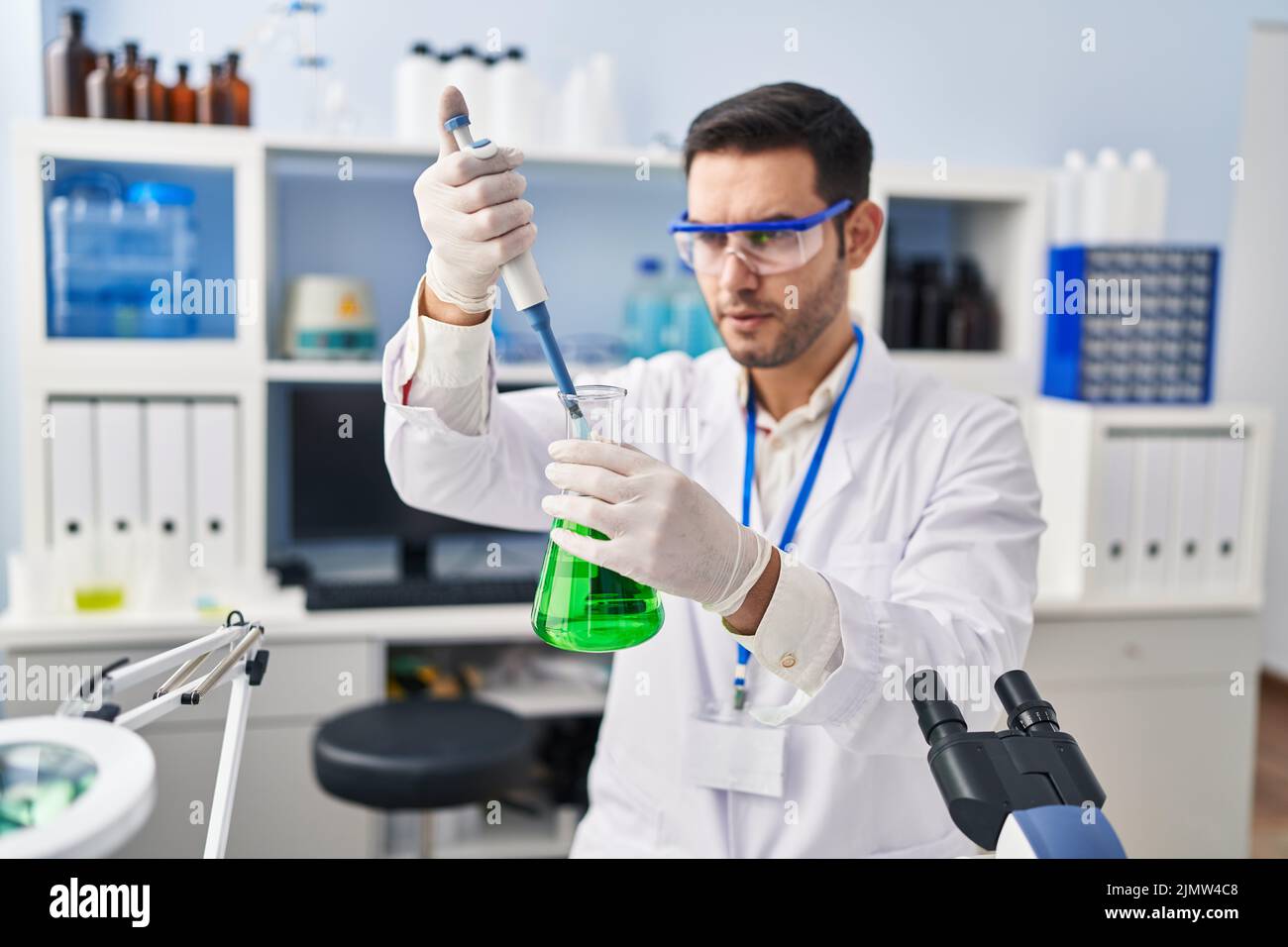 Young hispanic man scientist measuring liquid using pipette at ...