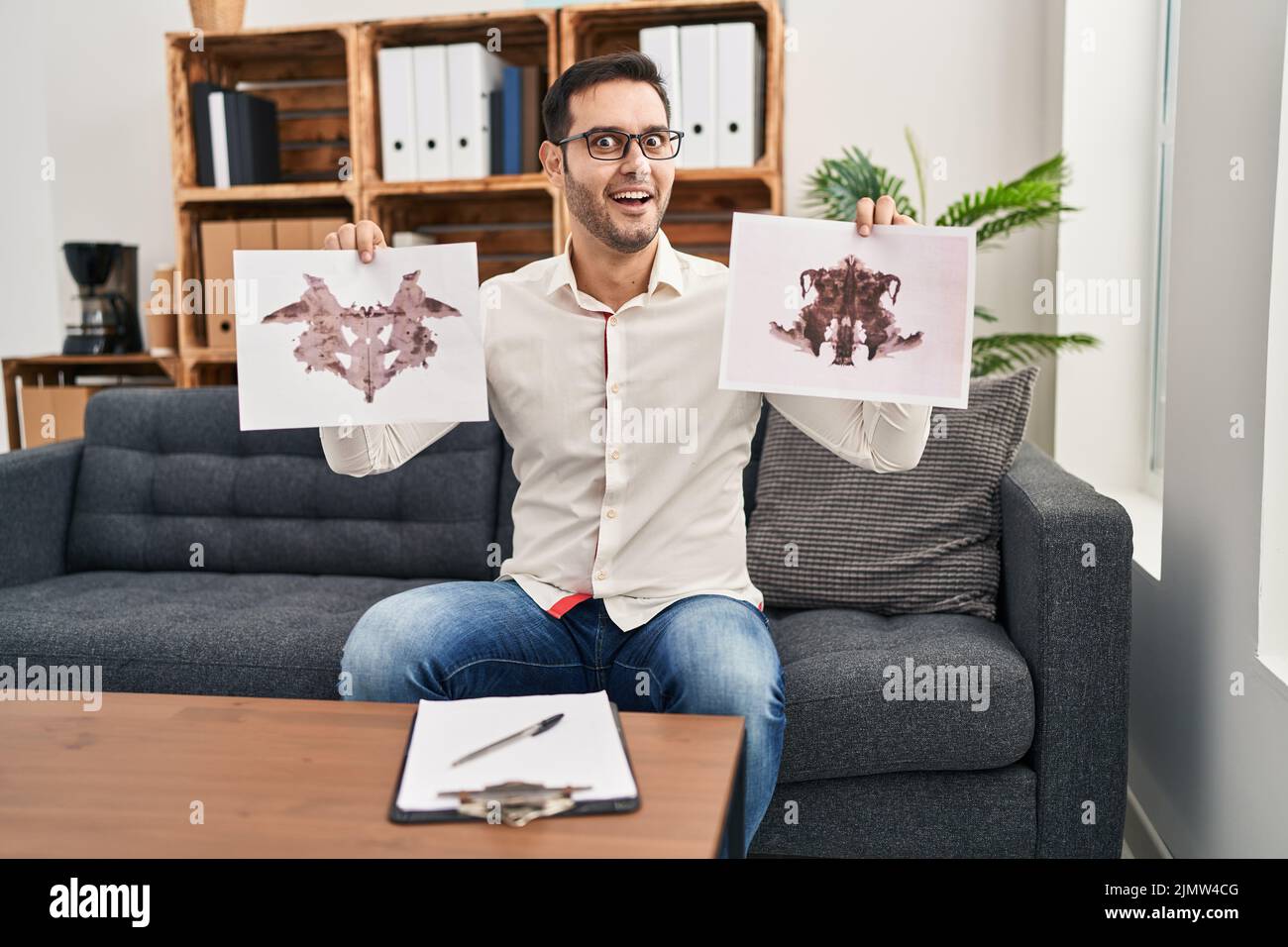 Young hispanic man with beard holding rorschach test celebrating crazy ...
