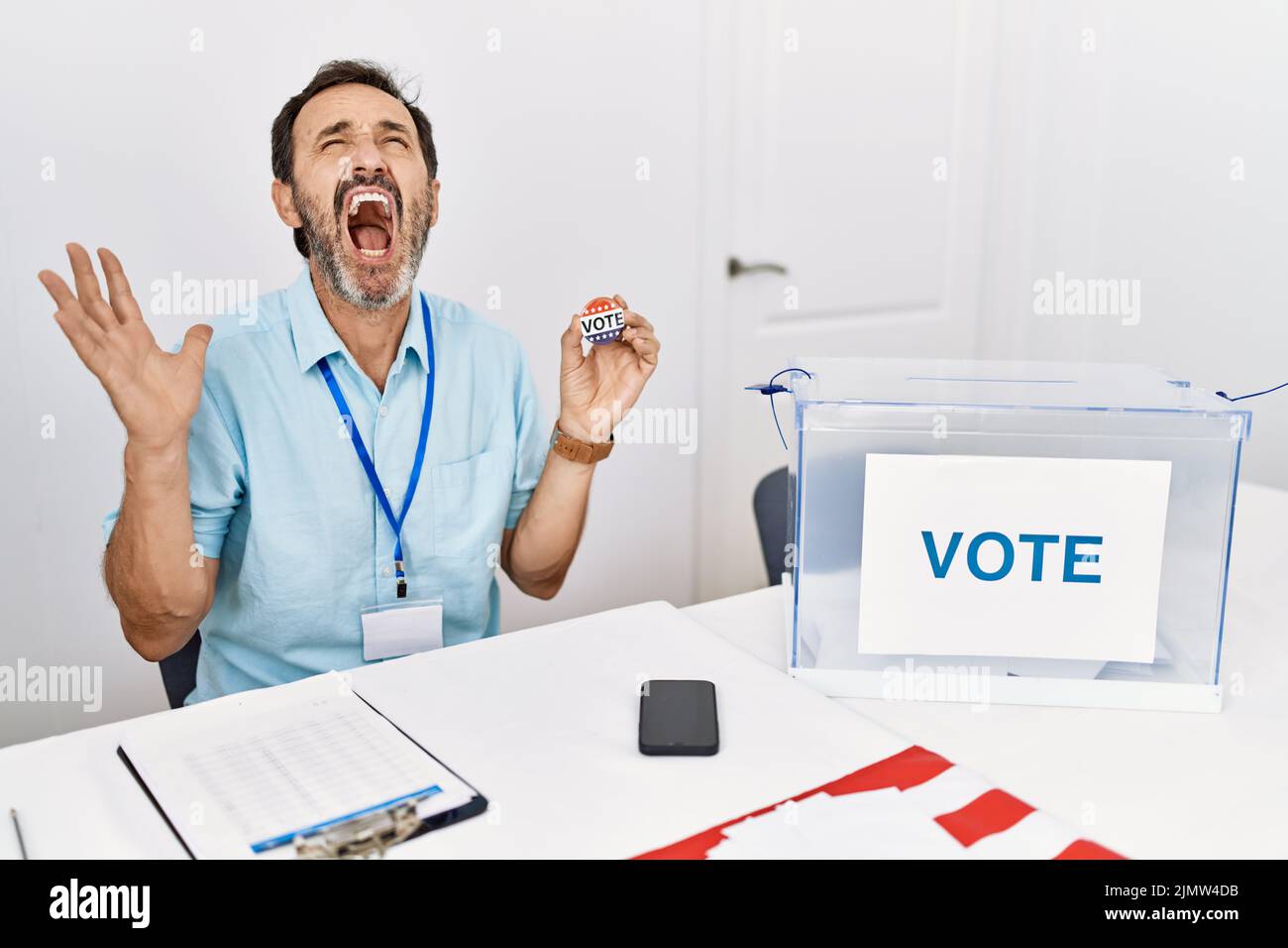 Middle age man with beard sitting by ballot holding i vote badge crazy ...