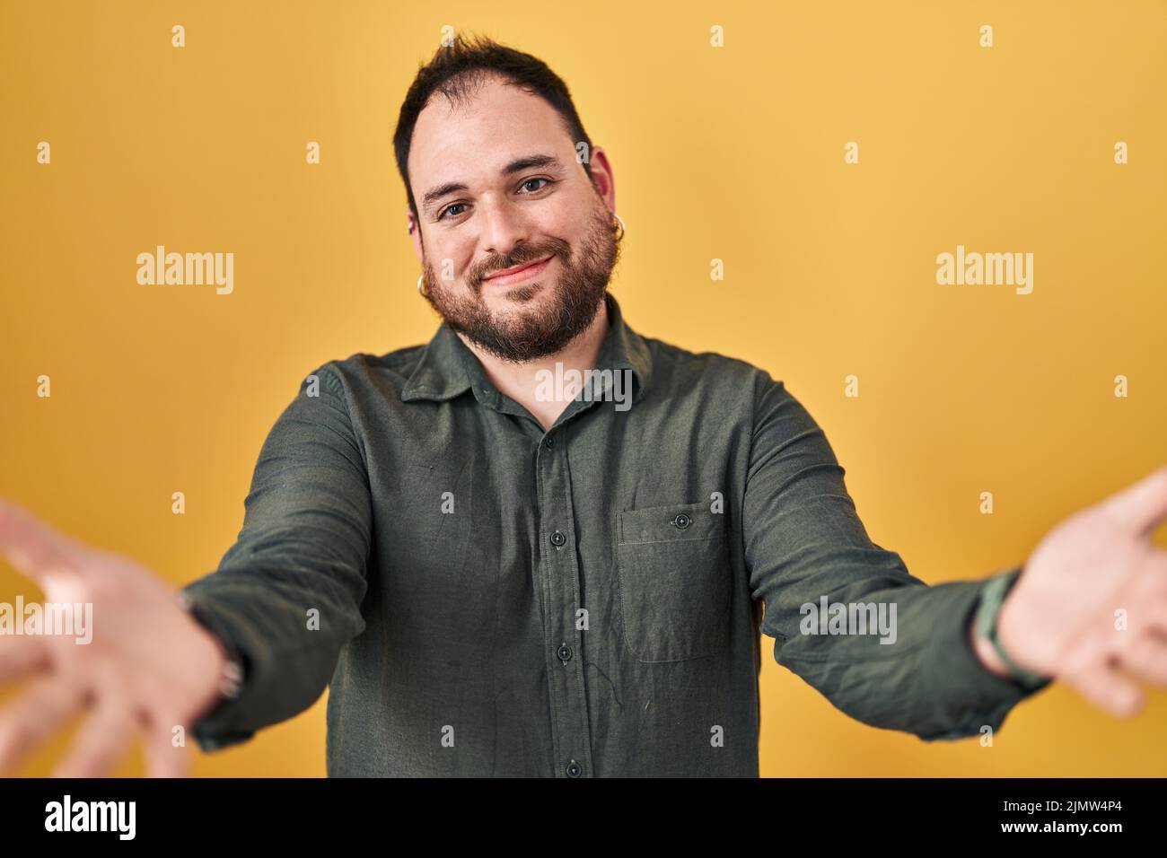 Plus size hispanic man with beard standing over yellow background ...