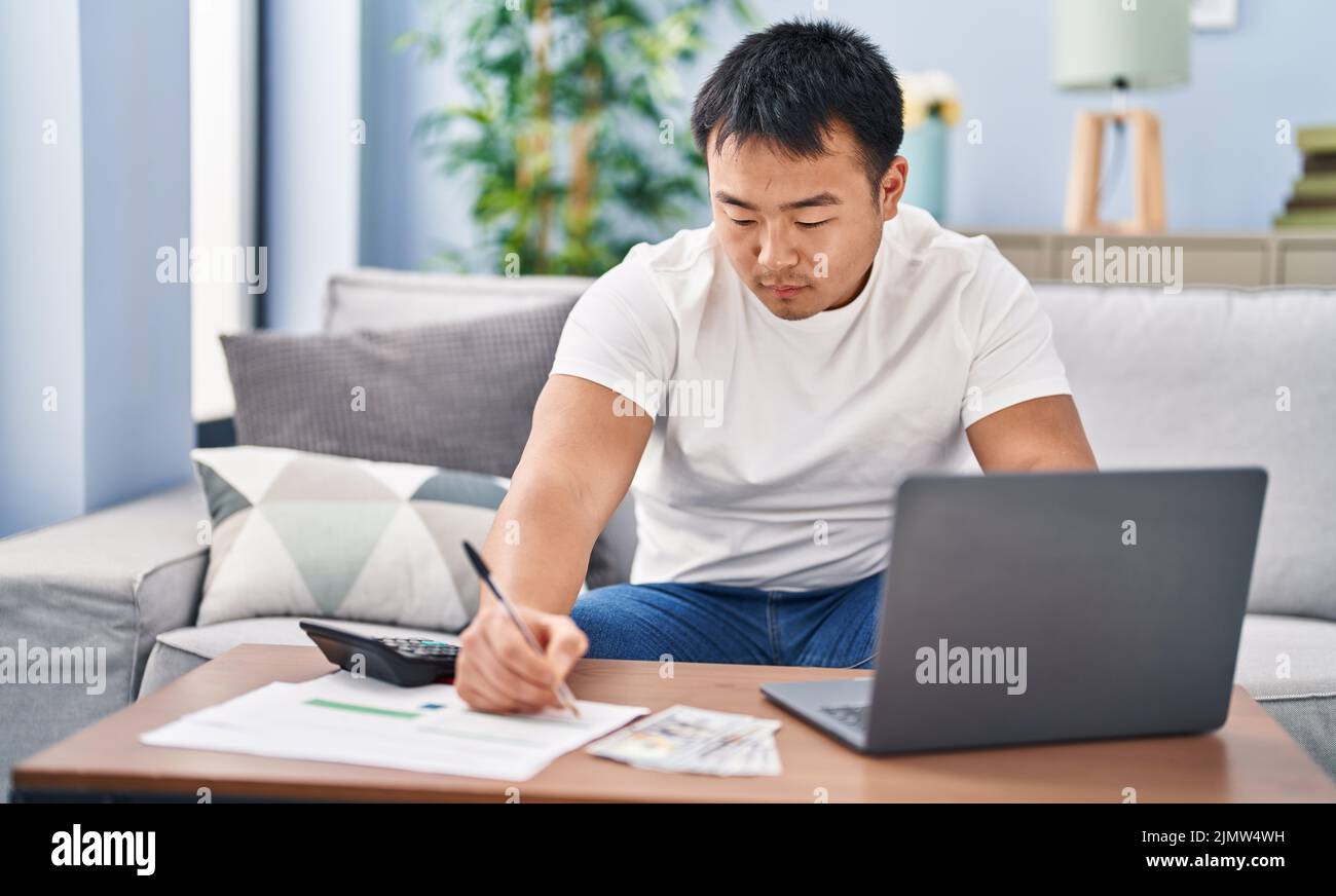 Young chinese man accounting economy using laptop and calculator at ...