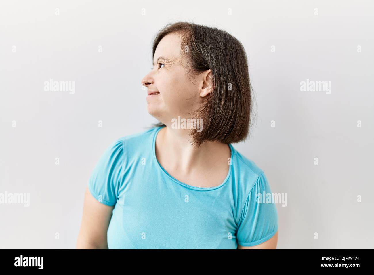 Young down syndrome woman standing over isolated background looking ...