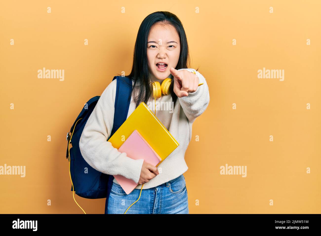 Young chinese girl holding student backpack and books pointing ...
