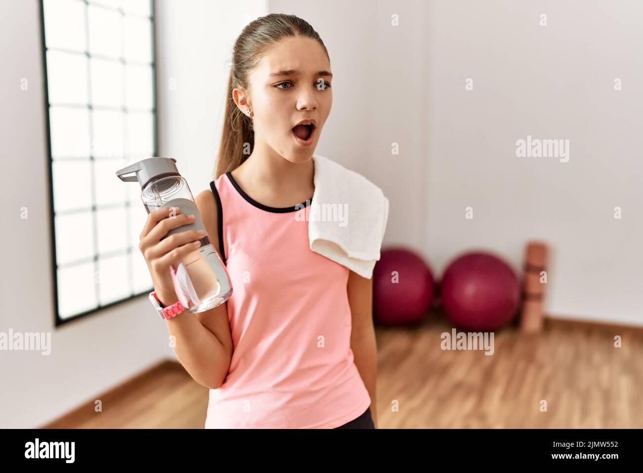 Young brunette teenager wearing sportswear holding water bottle angry ...
