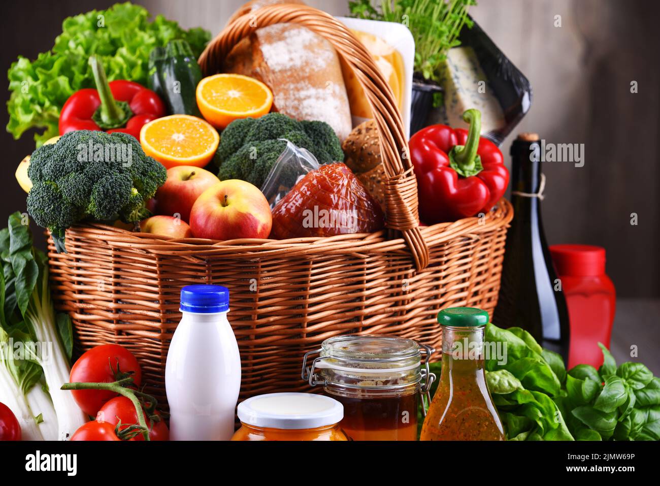 Wicker basket with assorted grocery products including fresh vegetables ...