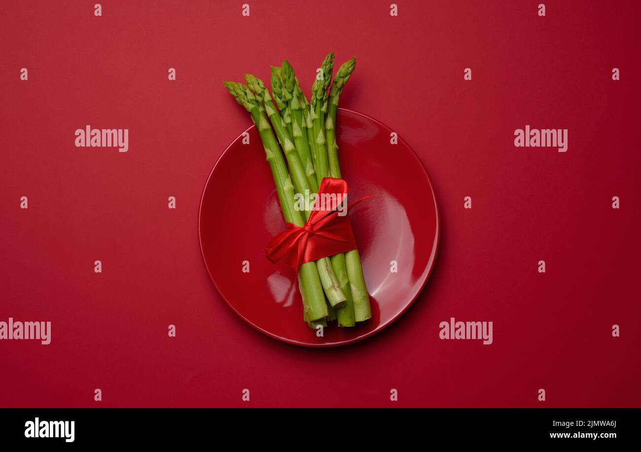Bunch of fresh asparagus in a red round plate on a red background, top ...