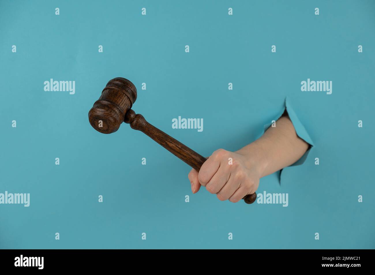 A woman's hand with a wooden judge's gavel sticks out of a hole in a ...