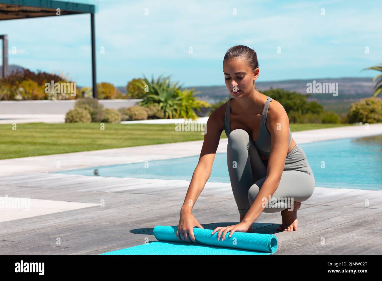 Caucasian young woman rolling her yoga mat near the pool Stock Photo ...