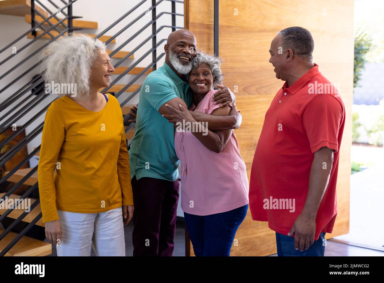 Happy multiracial seniors welcoming friends while standing at doorway ...