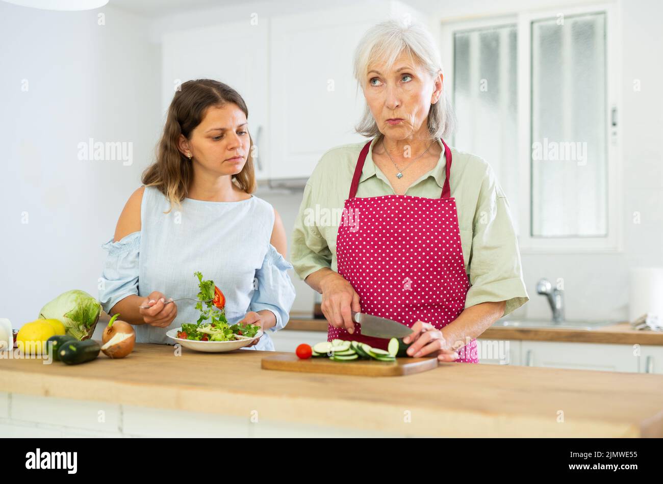 Elderly woman and her adult daughter making dinner together in kitchen ...