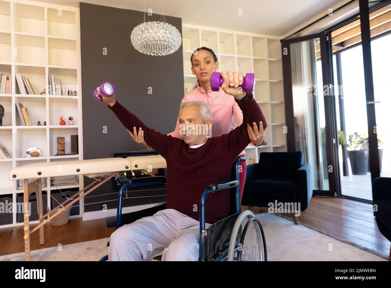 Biracial physiotherapist assisting senior caucasian man sitting on ...