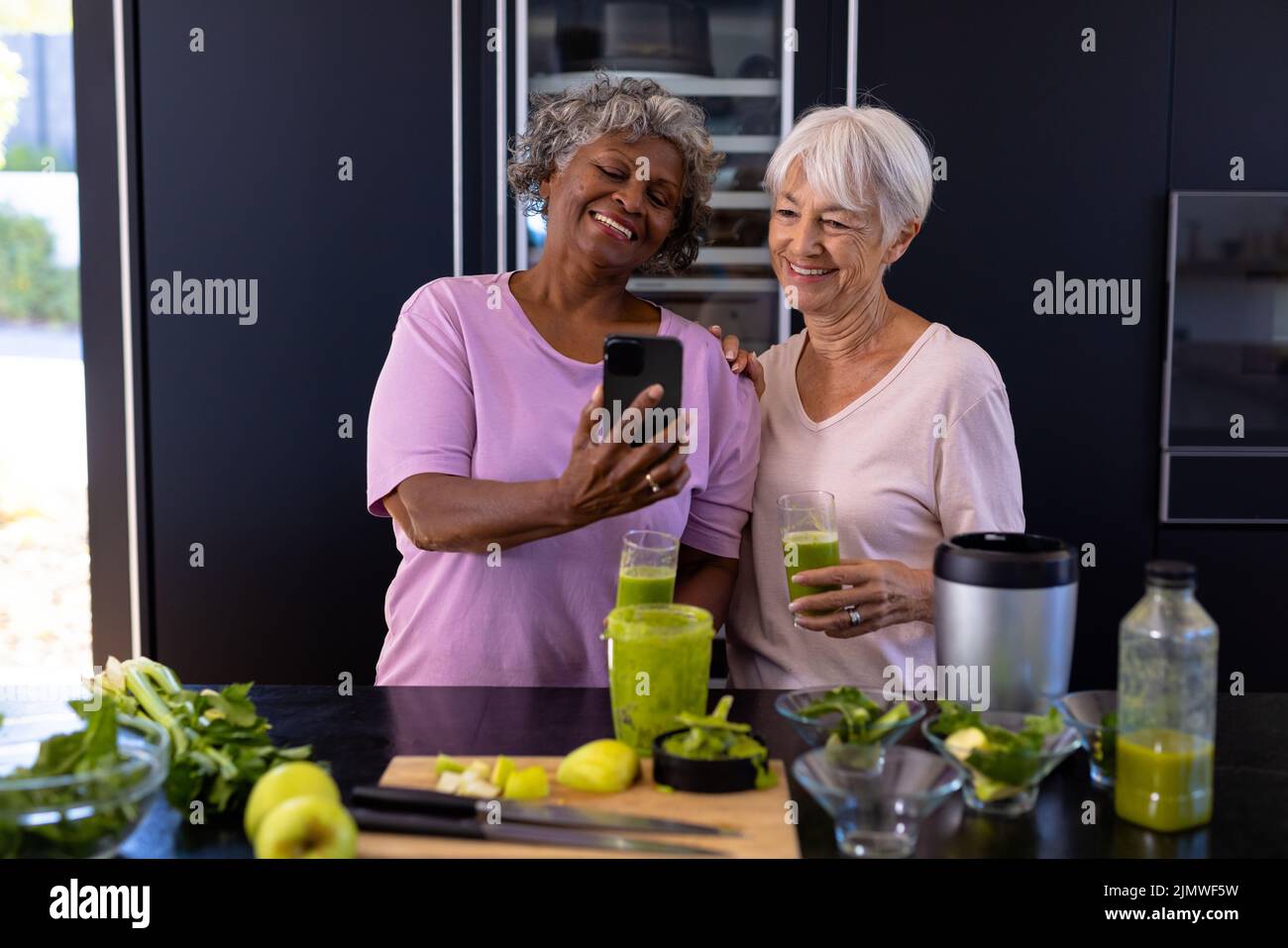 Smiling multiracial senior female friends looking at smartphone while ...