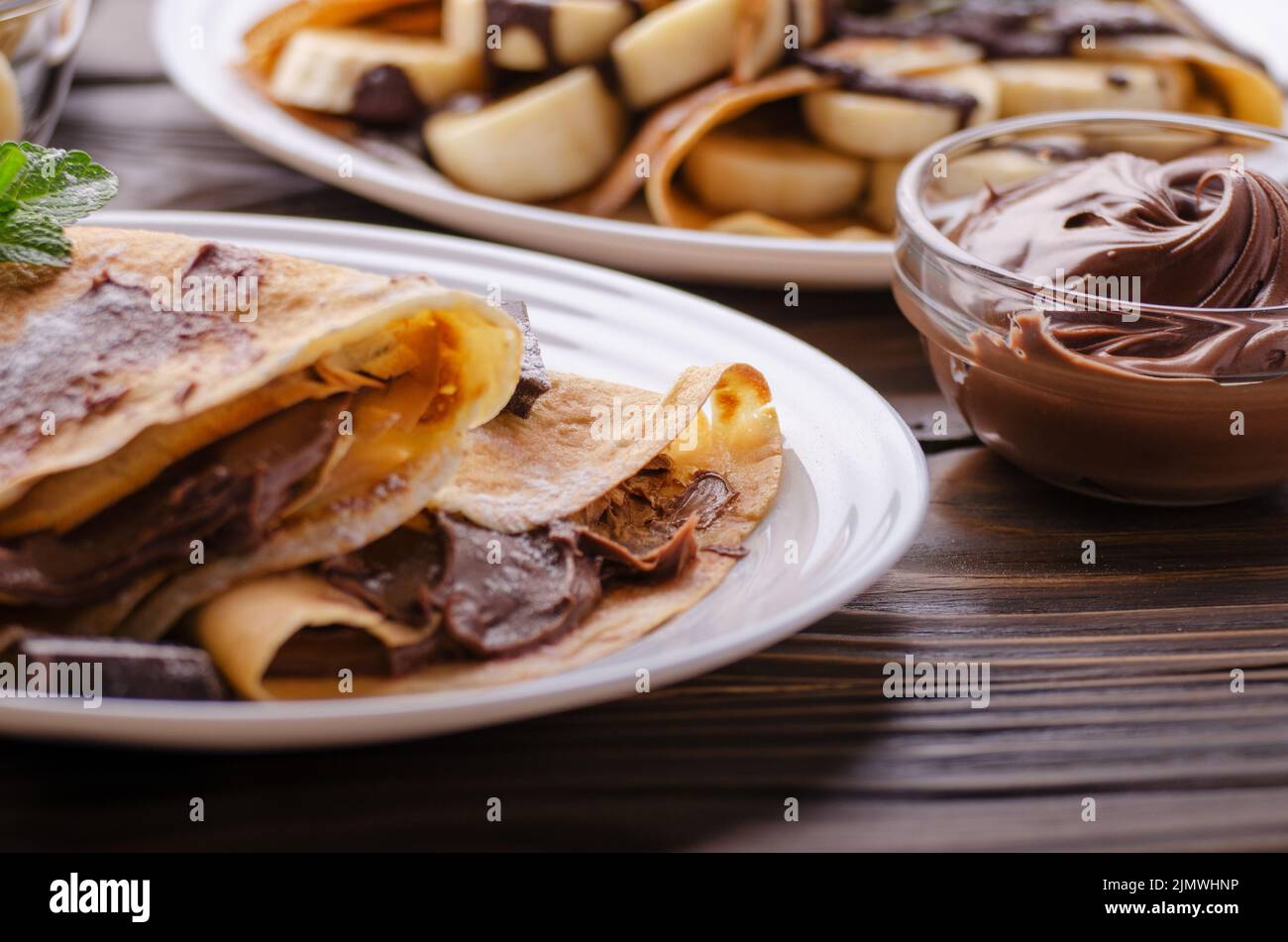 French crepes with chocolate sauce and banana in ceramic dish on wooden ...