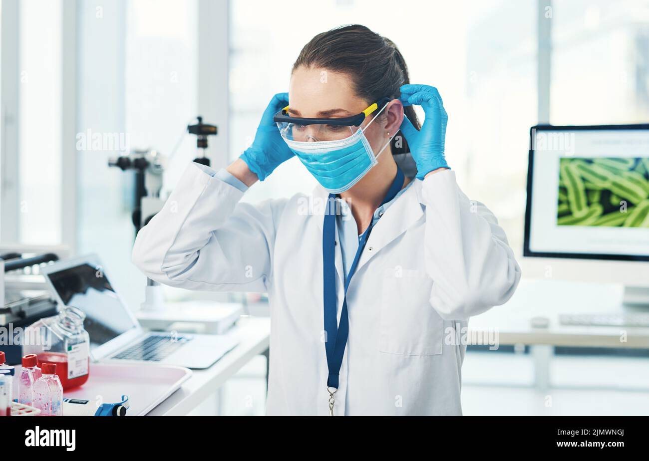 Safety first. an unrecognizable young female scientist putting on a ...