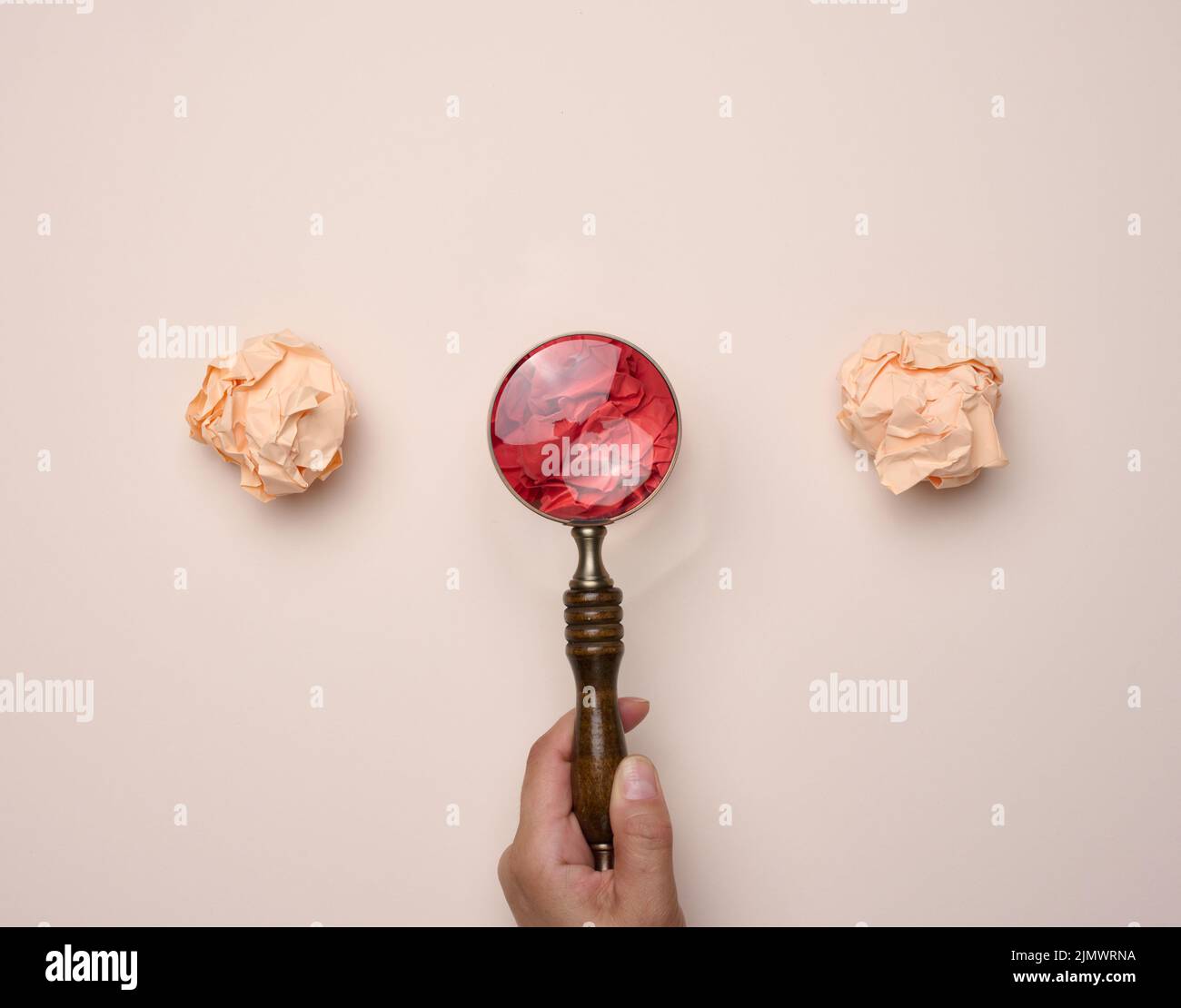 Female hand holds a wooden magnifying glass and crumpled balls of paper ...