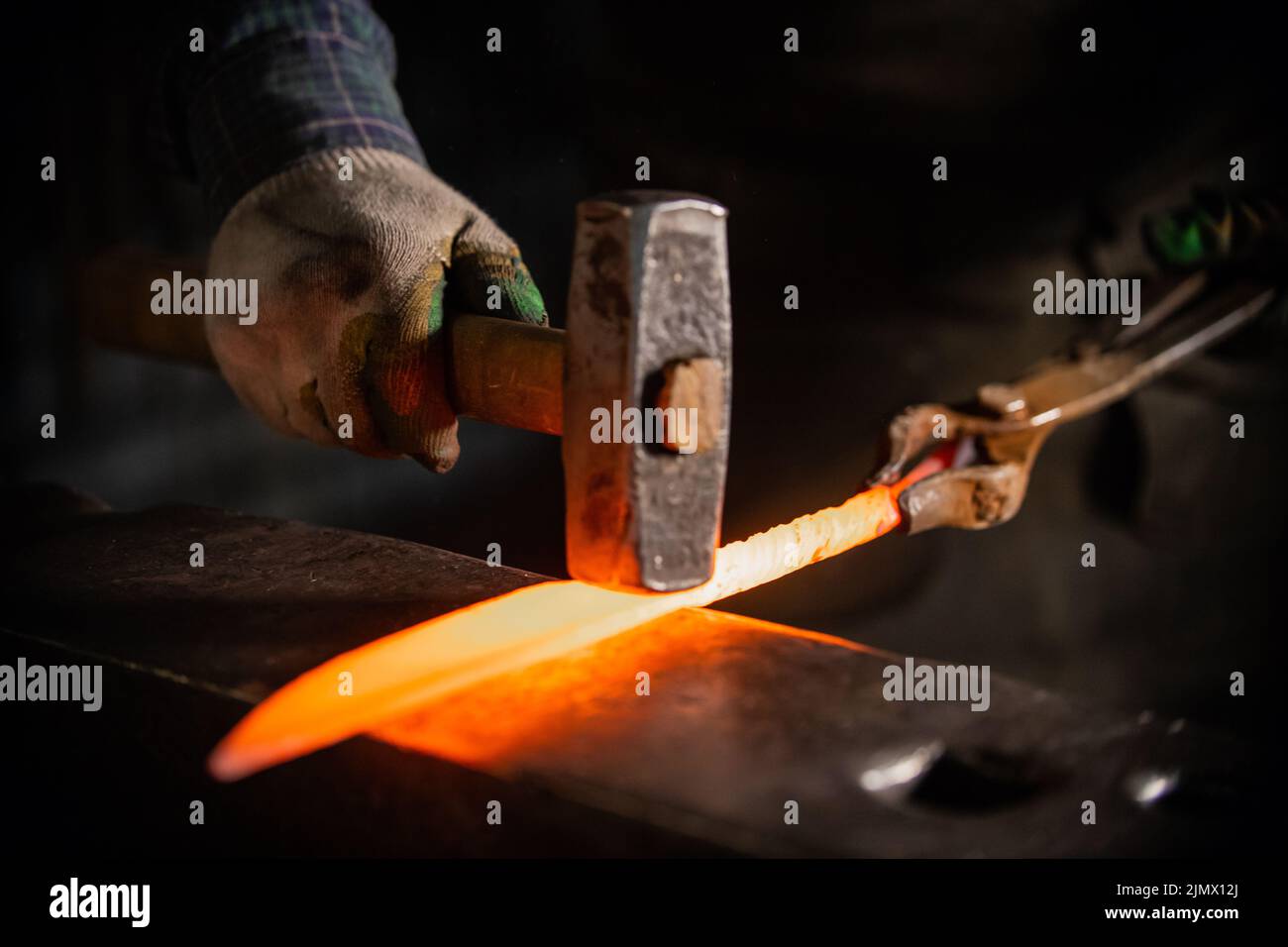 Forging a knife out of the hot metal using a hammer - holding the knife ...
