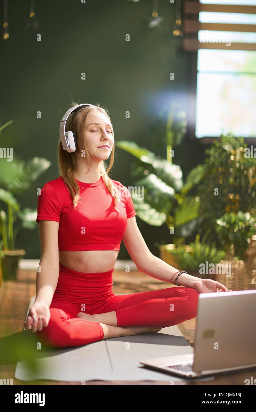 modern woman in red fitness clothes with laptop and headphones ...
