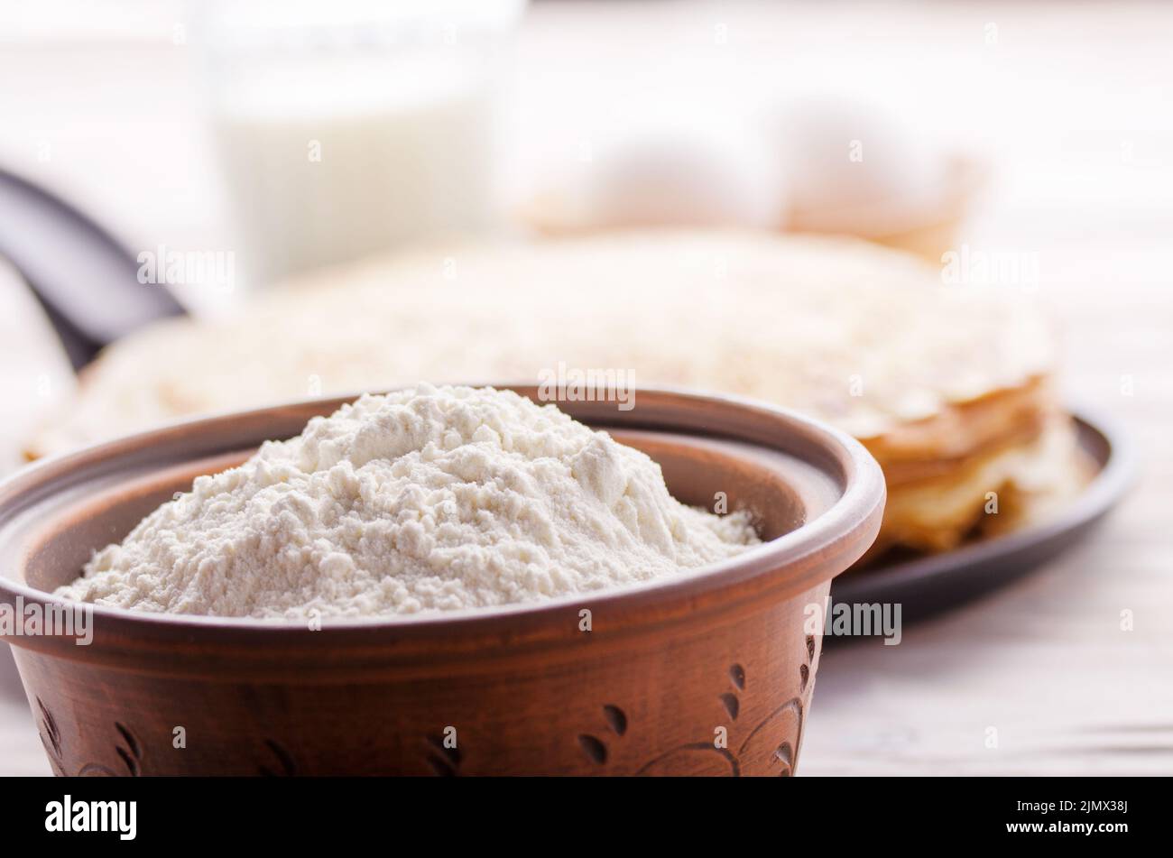 Stack of French crepes in frying pan on wooden kitchen table with milk ...