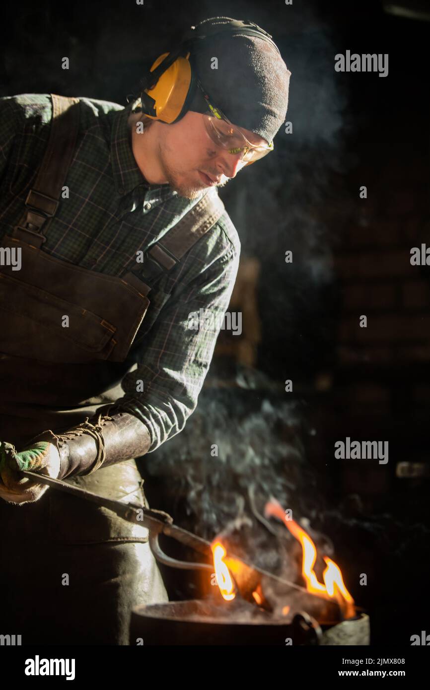 Blacksmith man worker putting a burning item in the bucket of water ...